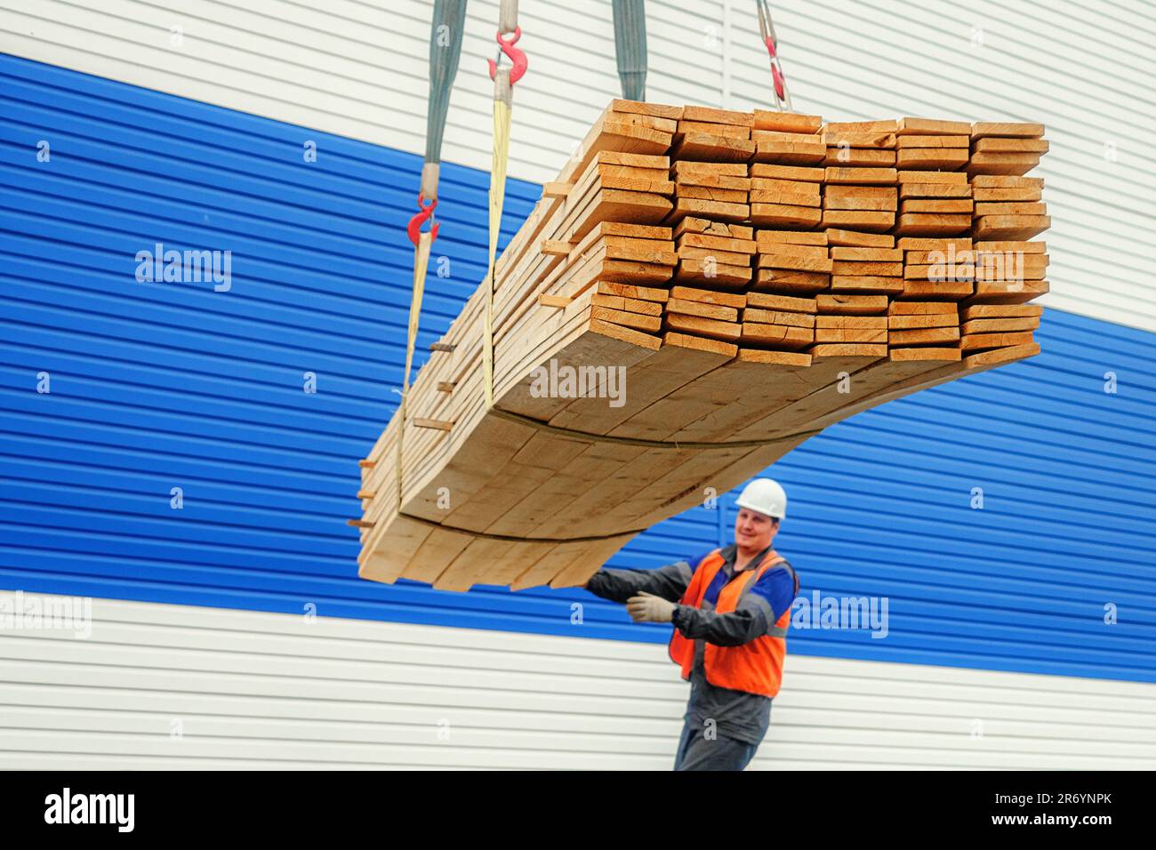 A slinger in a helmet and signal vest unloads wooden boards on the ...