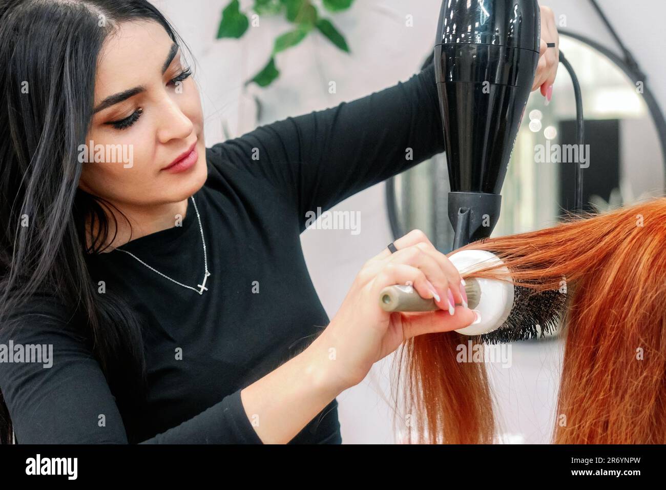 Beautiful woman stylist doing hair styling with hairdryer at client in ...