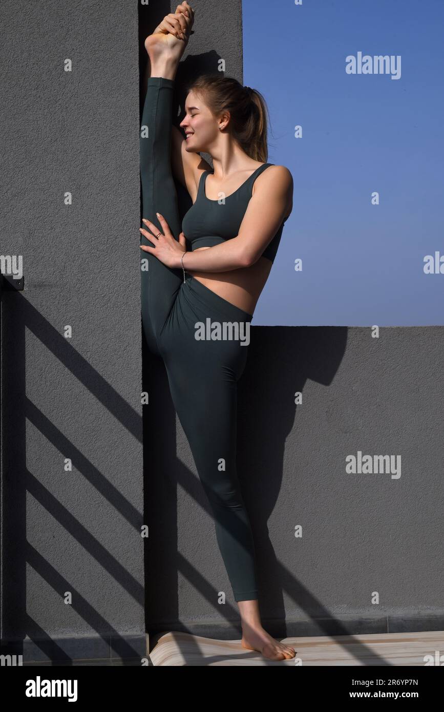 Young beautiful woman in sports outfits doing stretching before workout outdoor. Leg-split ...