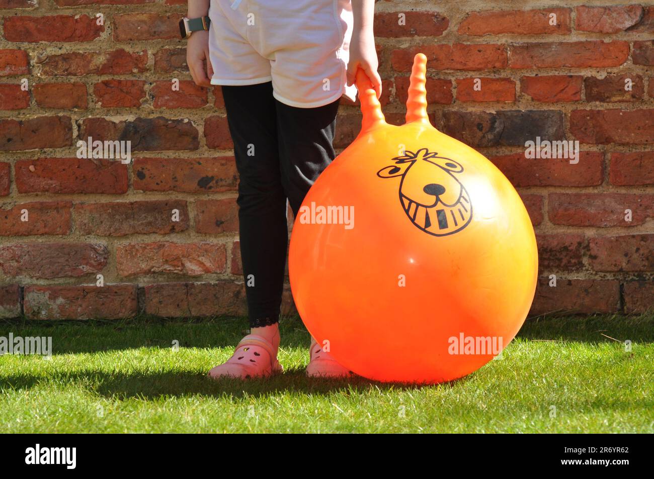 A young girl standing beside her space hopper in a garden on a summer ...