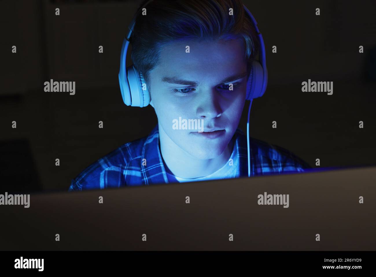 Teenage boy in headphones using computer at night. Internet addiction ...