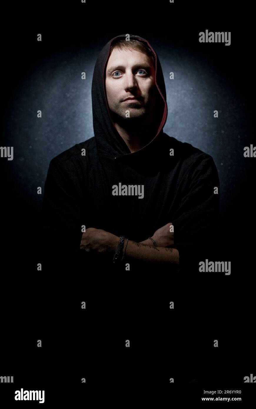Portrait of young man with a hood, on black backdrop with only his face ...