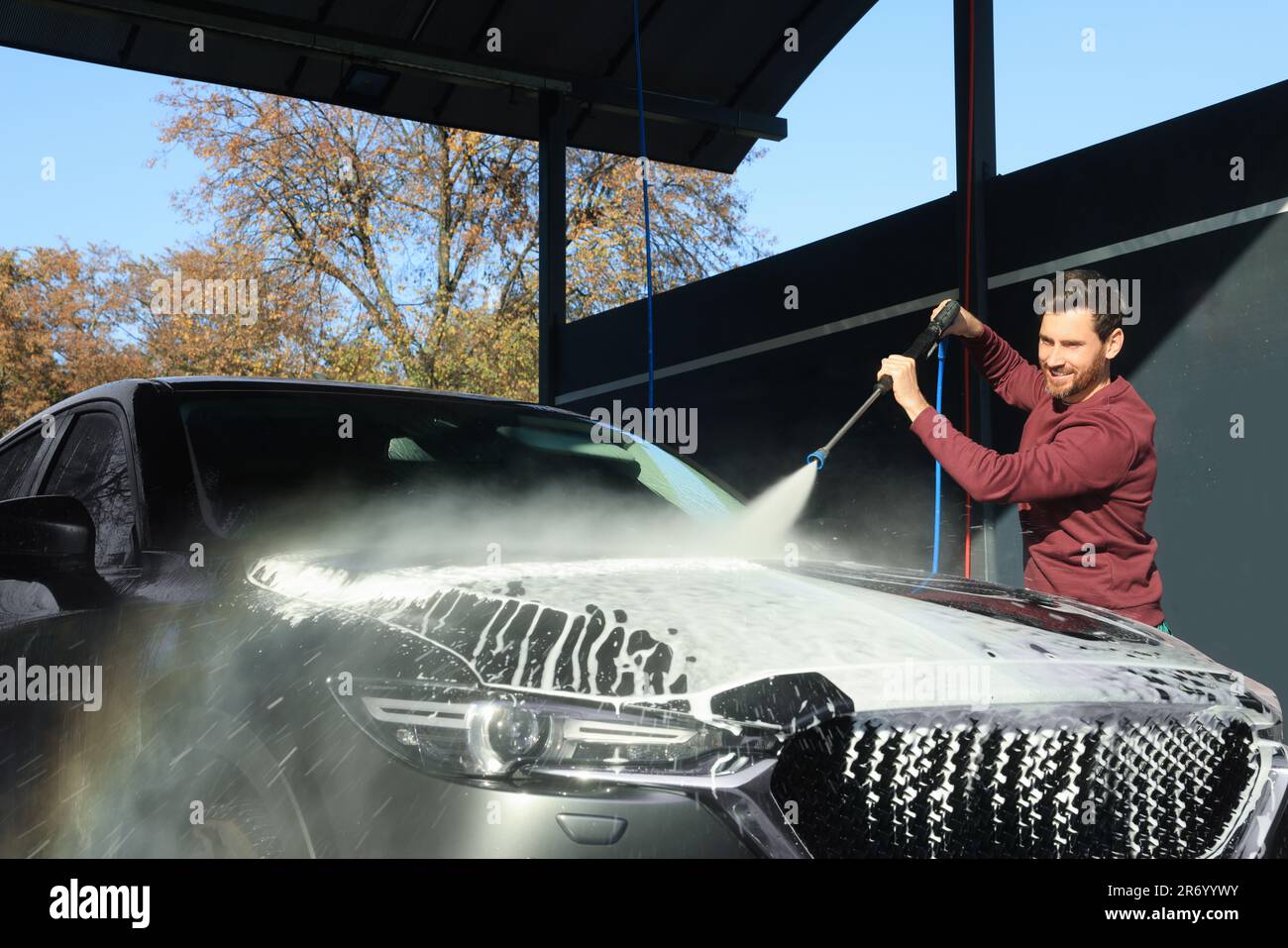 Worker washing auto with high pressure water jet at outdoor car wash ...