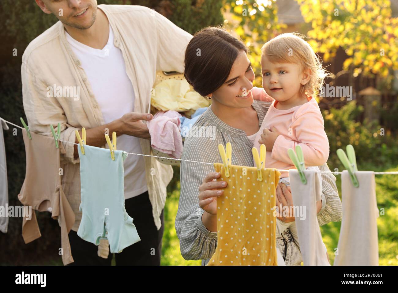 Happy family hanging baby clothes with clothespins on washing line for ...