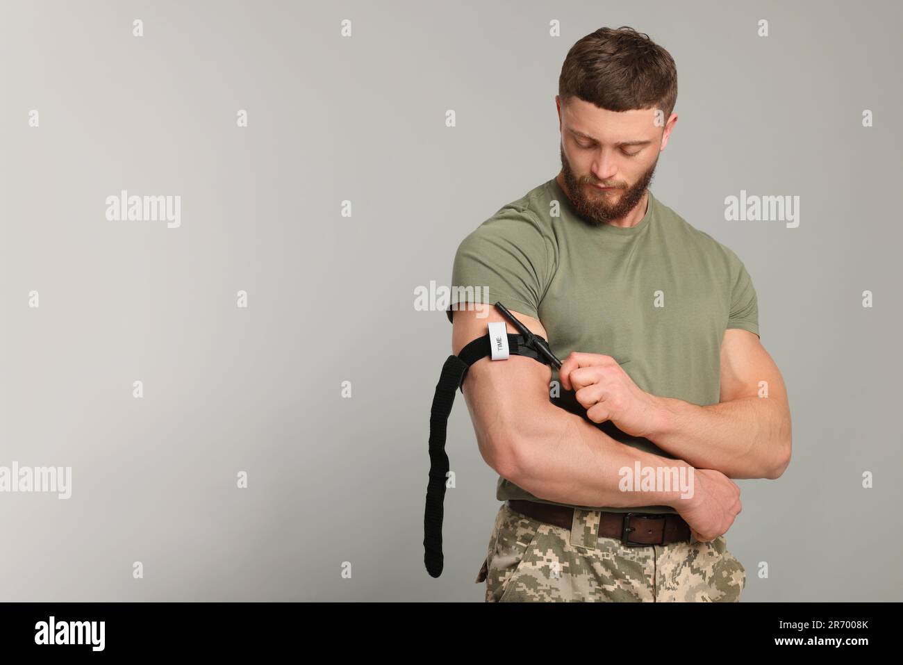 Soldier in military uniform applying medical tourniquet on arm against ...