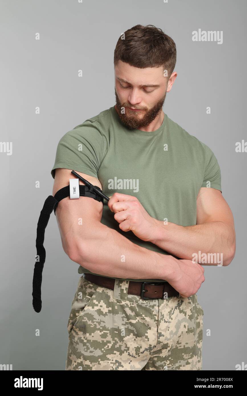 Soldier in military uniform applying medical tourniquet on arm against ...