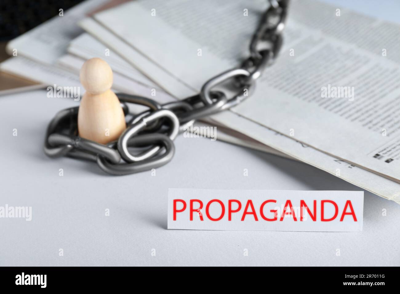 Propaganda concept. Chained wooden figure and newspapers on table Stock ...