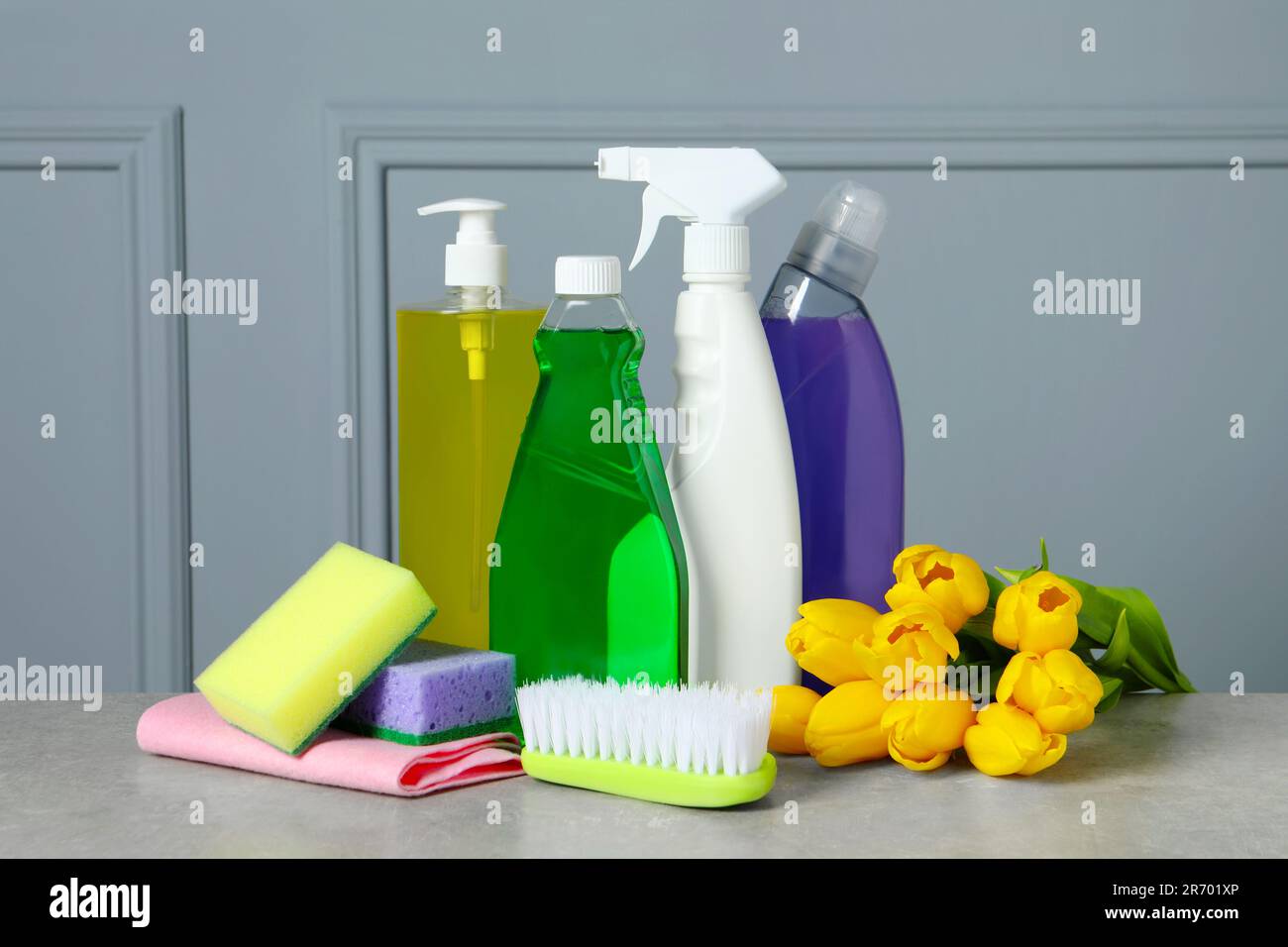 Spring cleaning. Detergents, flowers and tools on grey textured table ...