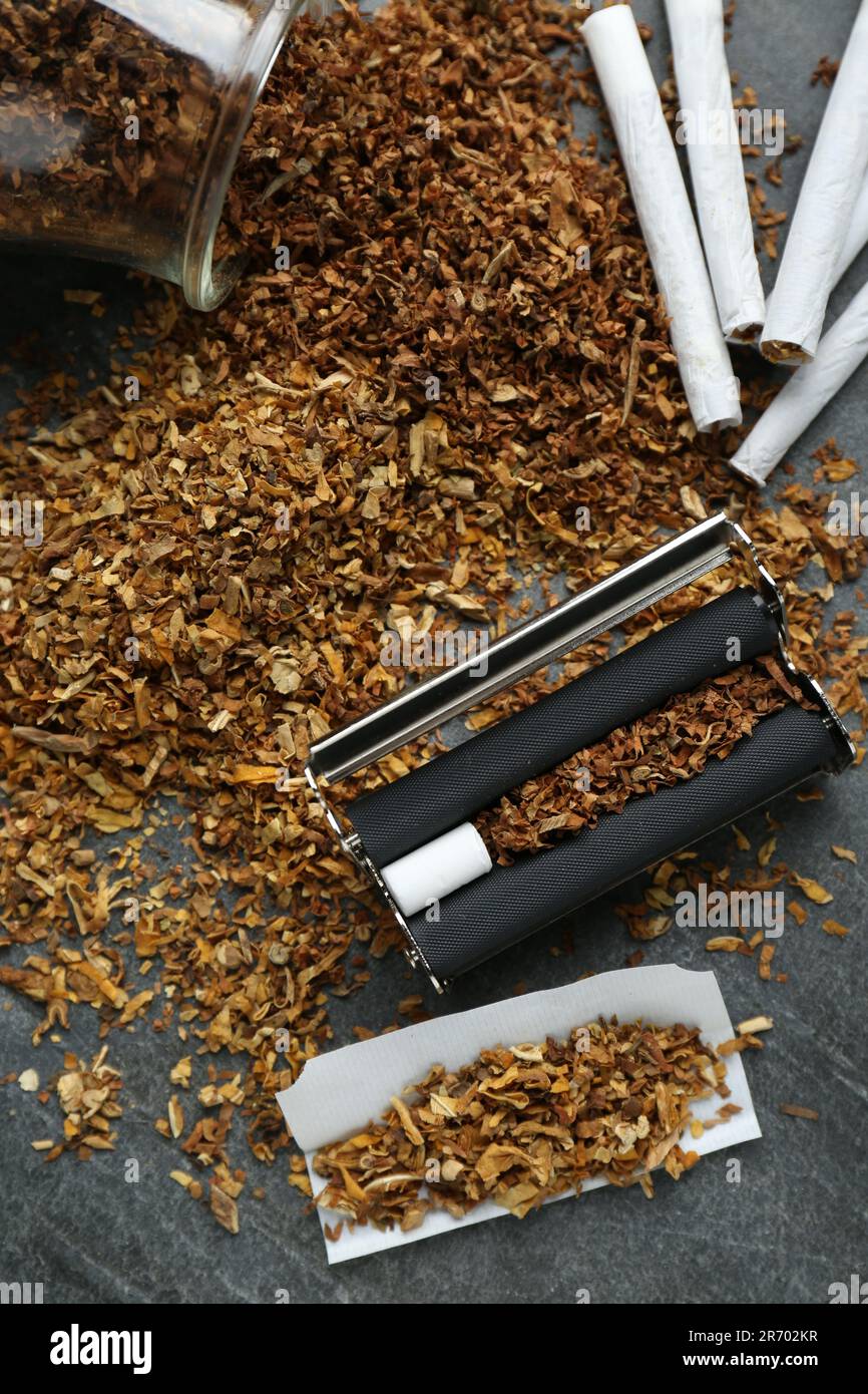 Flat lay composition with roller and tobacco on dark grey table. Making ...