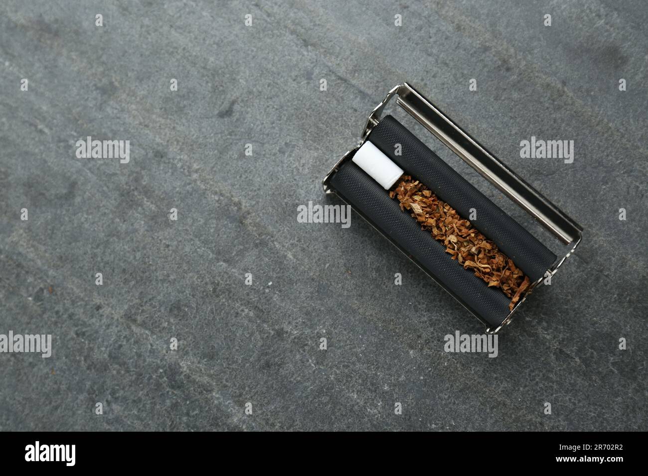 Cigarette roller with tobacco and filter on grey table, top view. Space ...