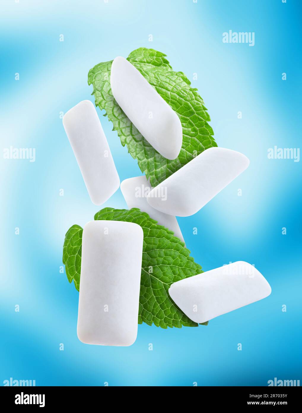 Fresh mint leaves and chewing gum pads falling on light blue background ...