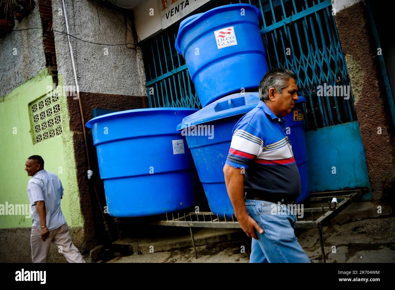 Men walk past bright blue water tanks for sale in a slum in Caracas ...
