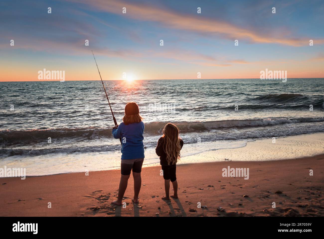 Two little girls fishing in the ocean at sunset Stock Photo - Alamy