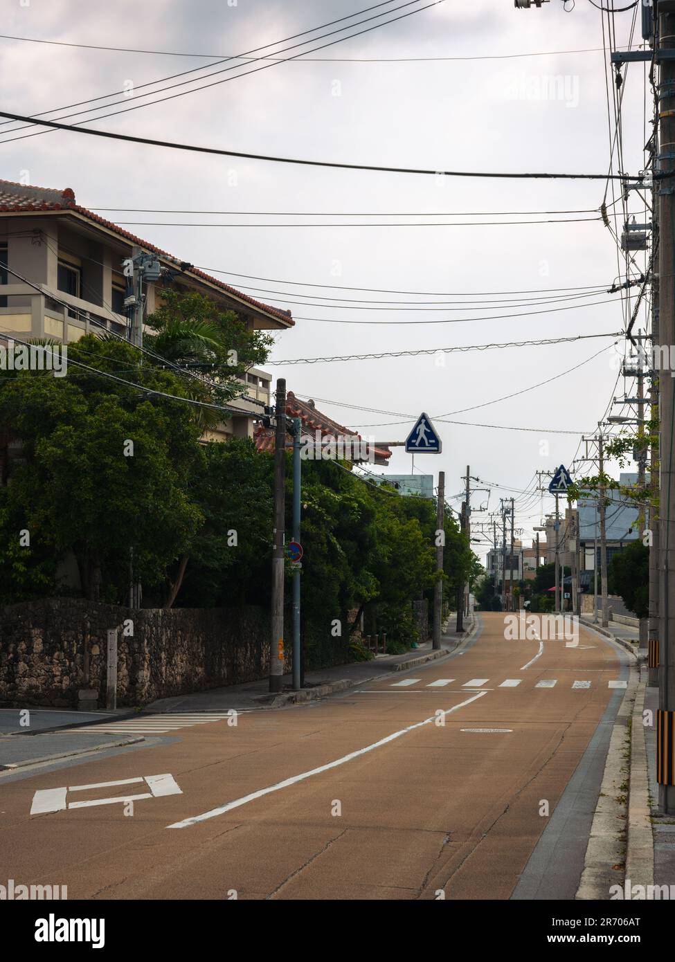 An empty city street in Okinawa, Japan, lined with trees and buildings ...