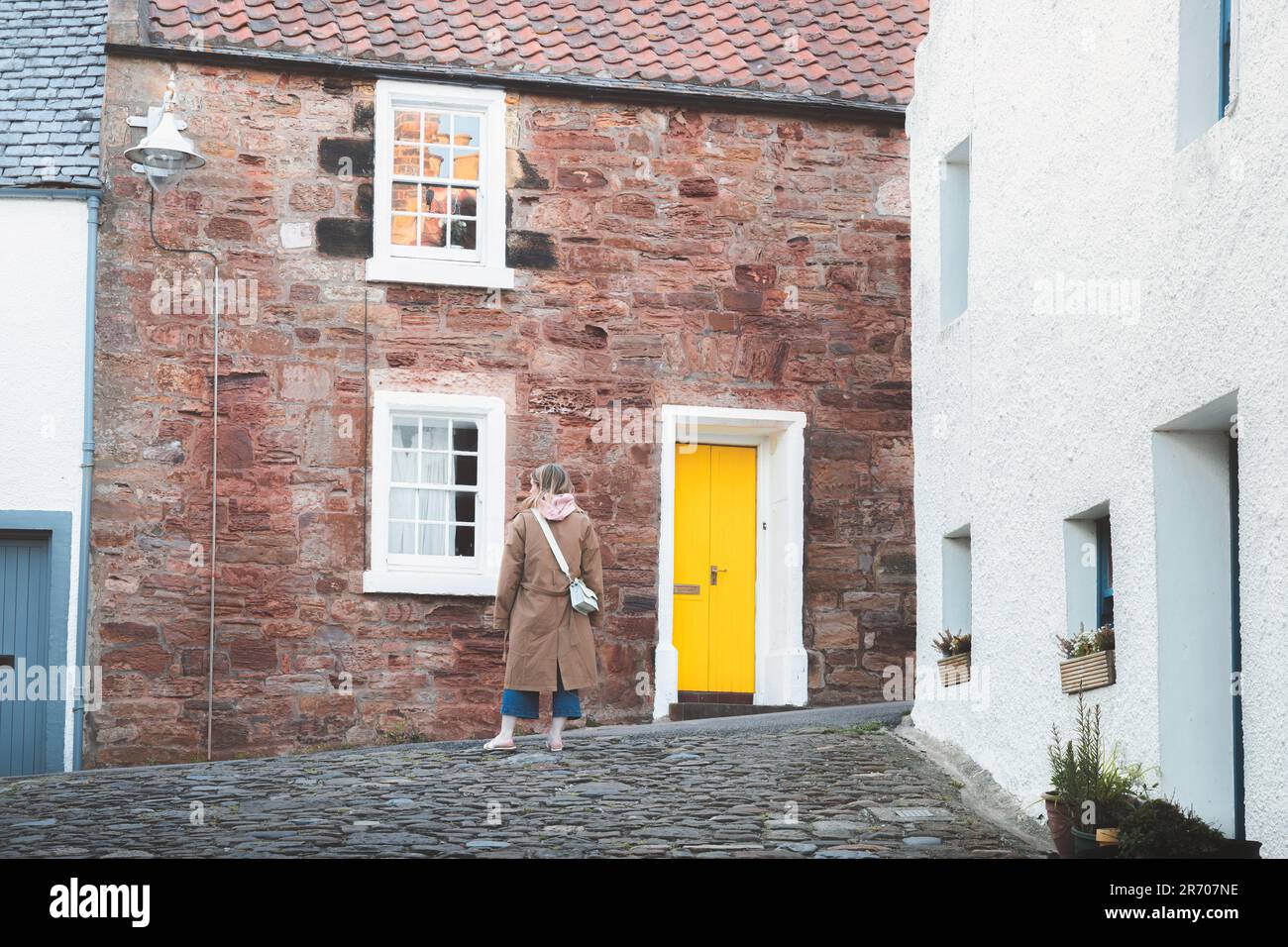 A young blonde female tourist explores a quiet cobblestone lane in the ...