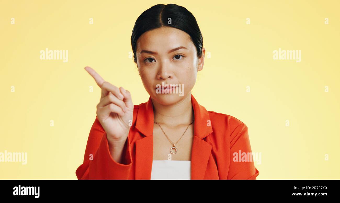 Face, warning and Asian woman serious, finger and stop against a studio ...