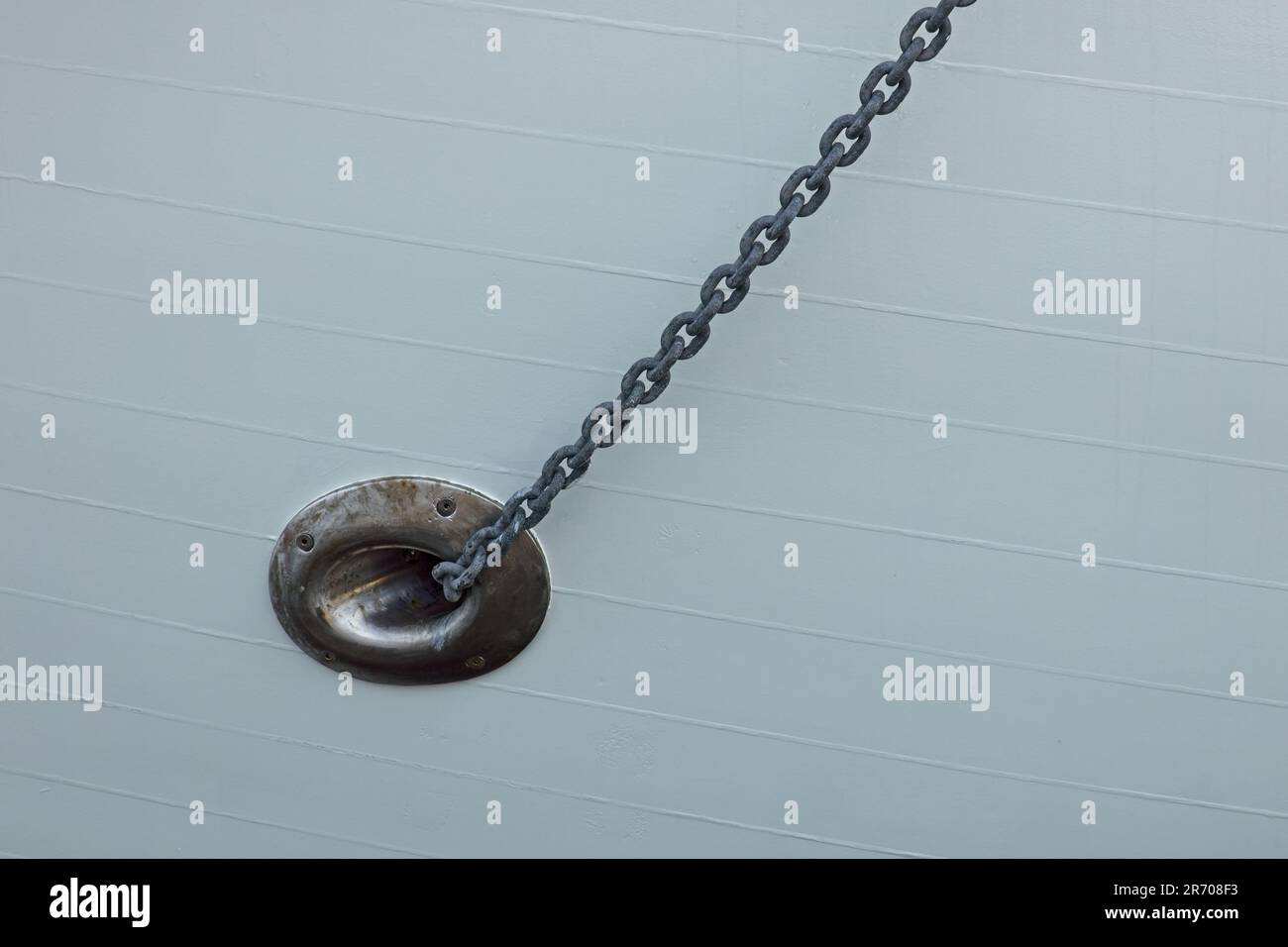 A mooring rope coming out of the hole in the side of a old metal ship ...