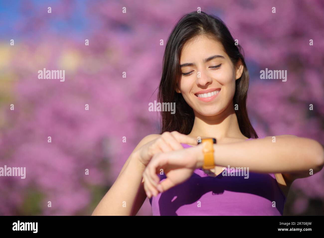 Front view portrait of a happy woman using smartwatch in a violet park ...