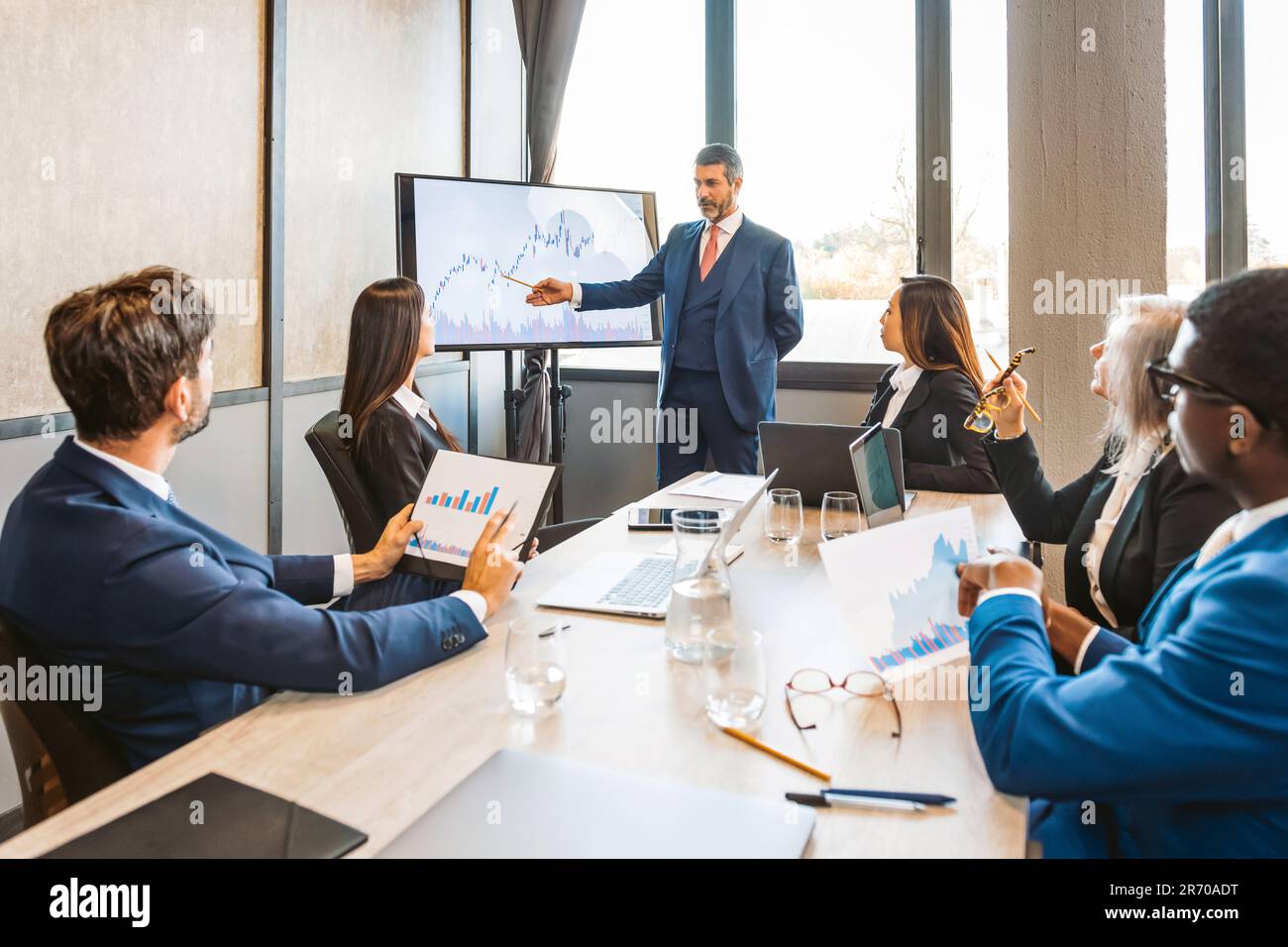 Male leader pointing at screen and explaining financial charts to coworkers during business ...