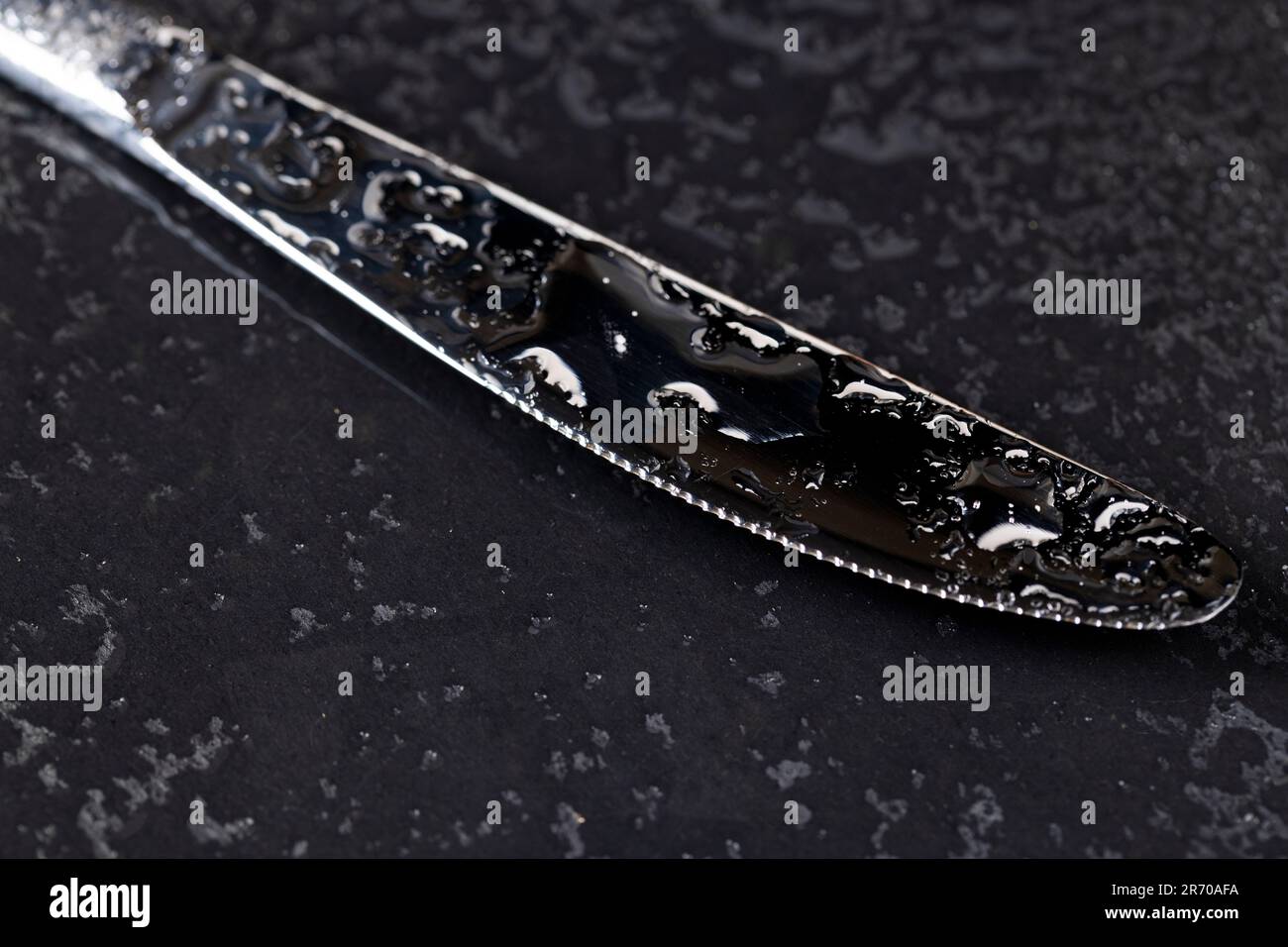 a steel knife covered with water droplets on black paper, a close-up of ...