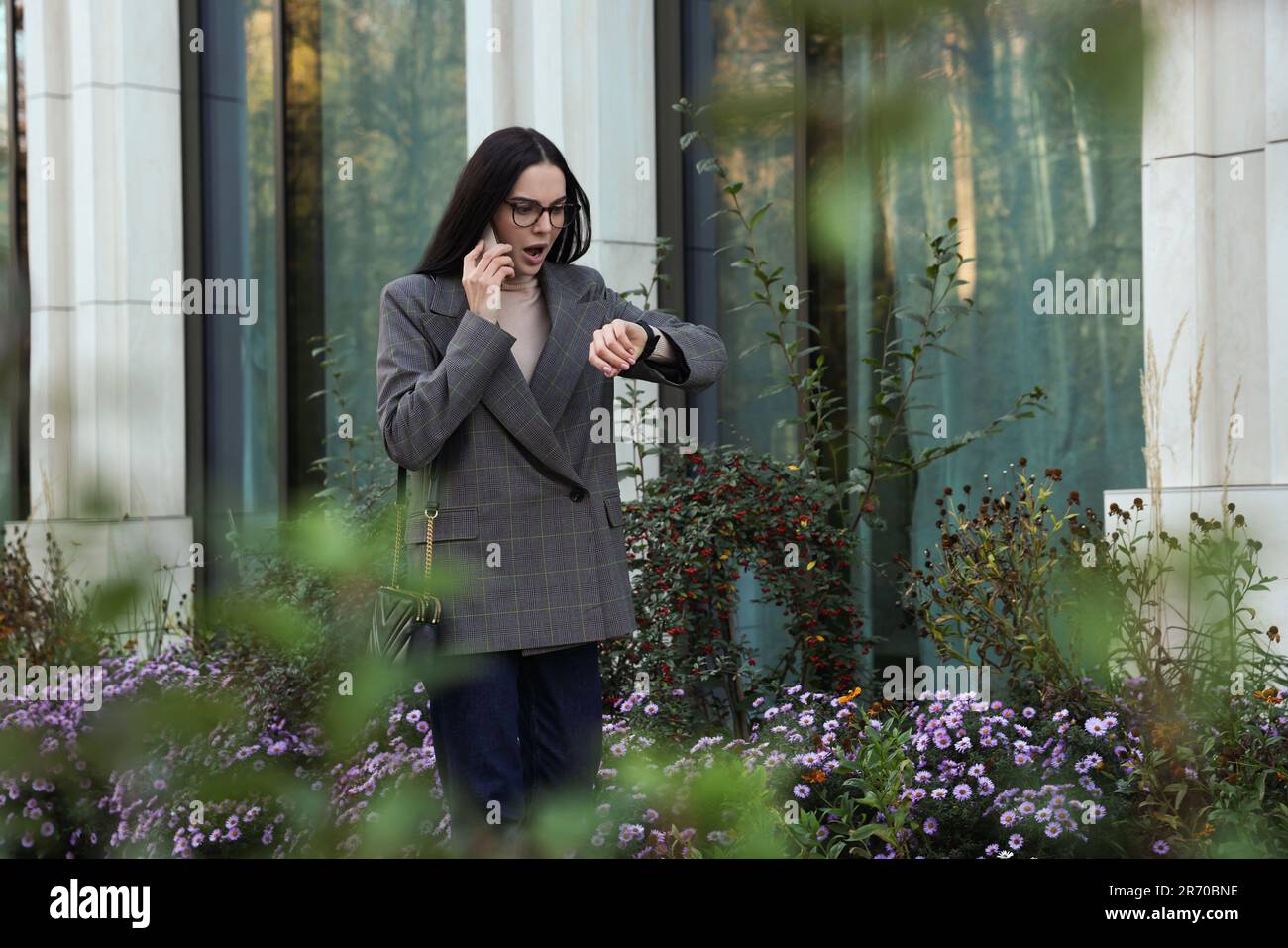 Emotional woman checking time while talking on smartphone outdoors ...
