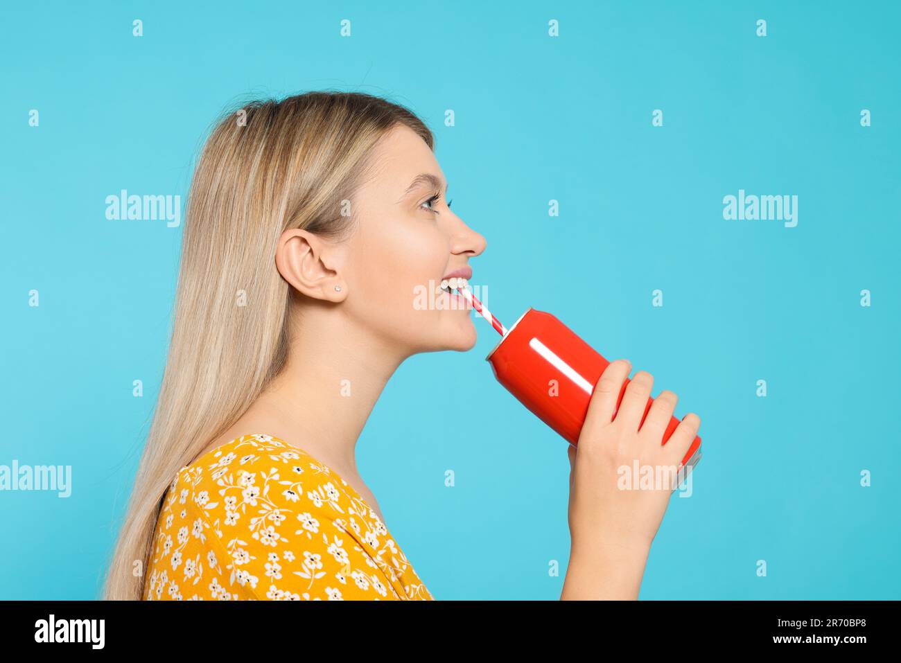 Beautiful happy woman drinking from red beverage can on light blue ...