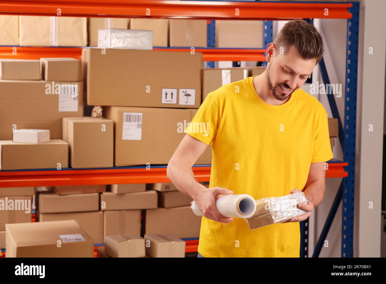 Post office worker wrapping parcel in stretch film indoors Stock Photo ...