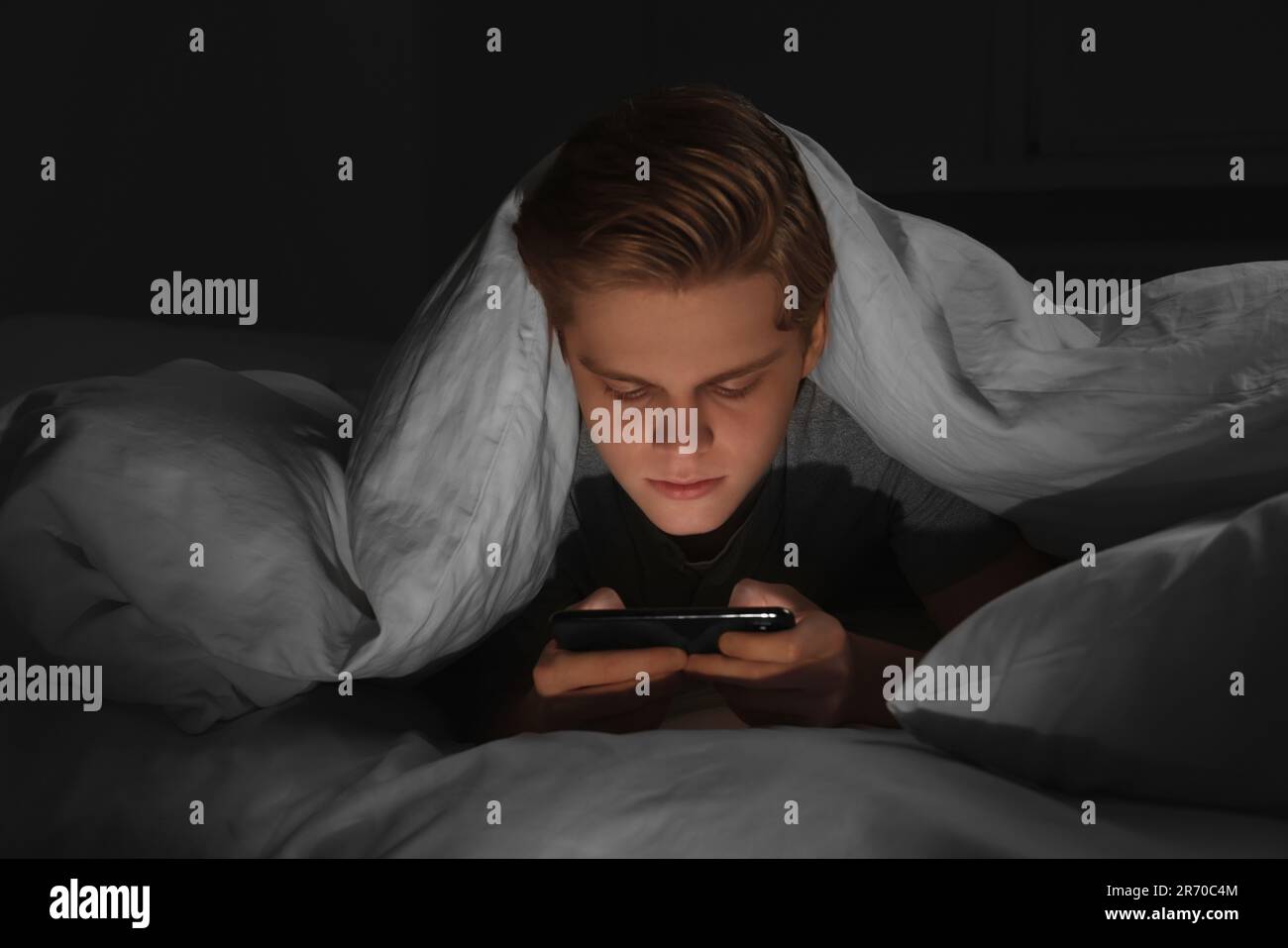 Teenage boy using smartphone under blanket on bed at night. Internet ...