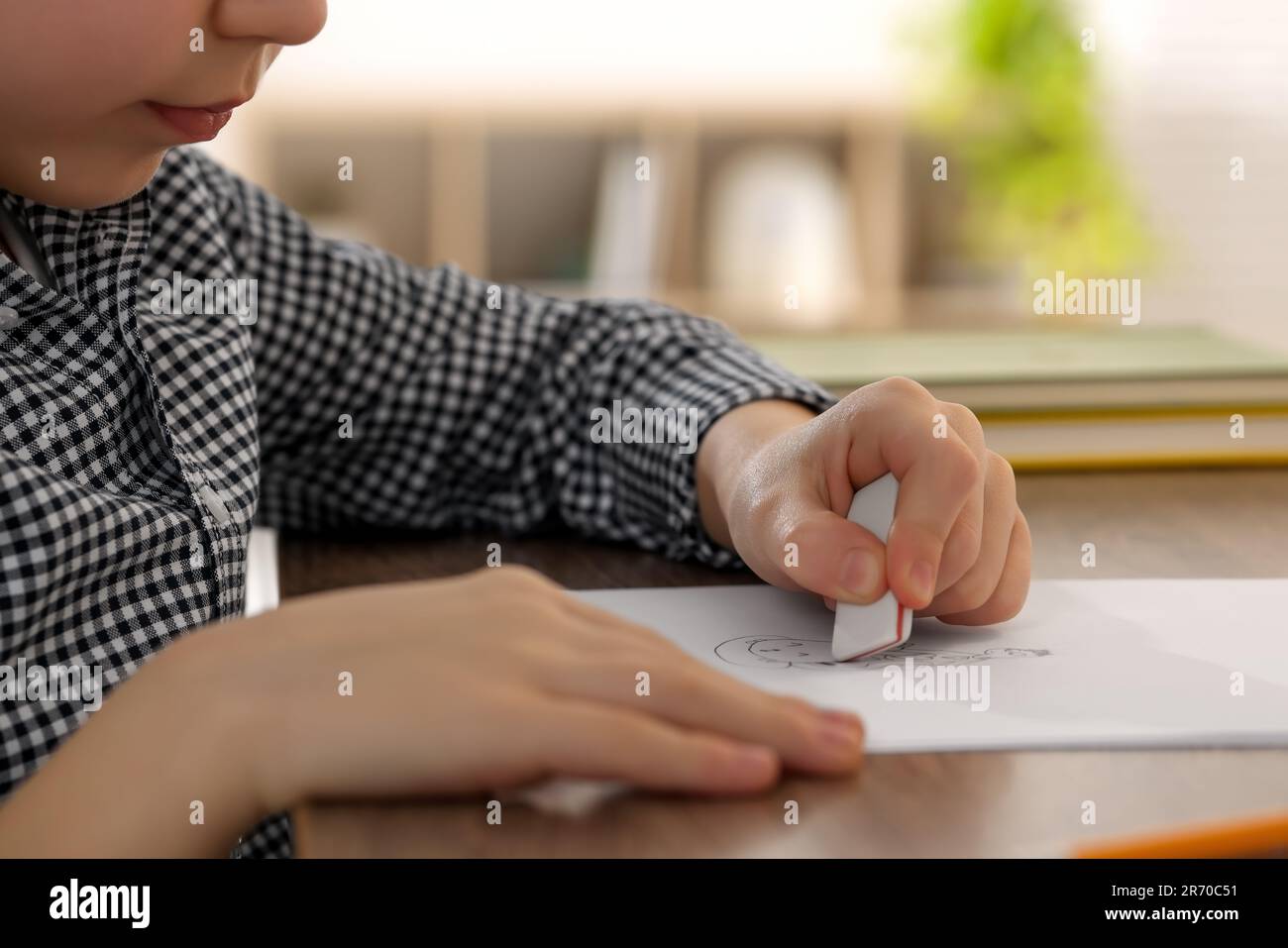 Little boy erasing mistake in his notebook at wooden desk indoors ...