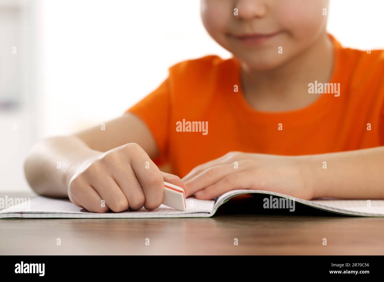 Little boy erasing mistake in his notebook at wooden desk, closeup ...