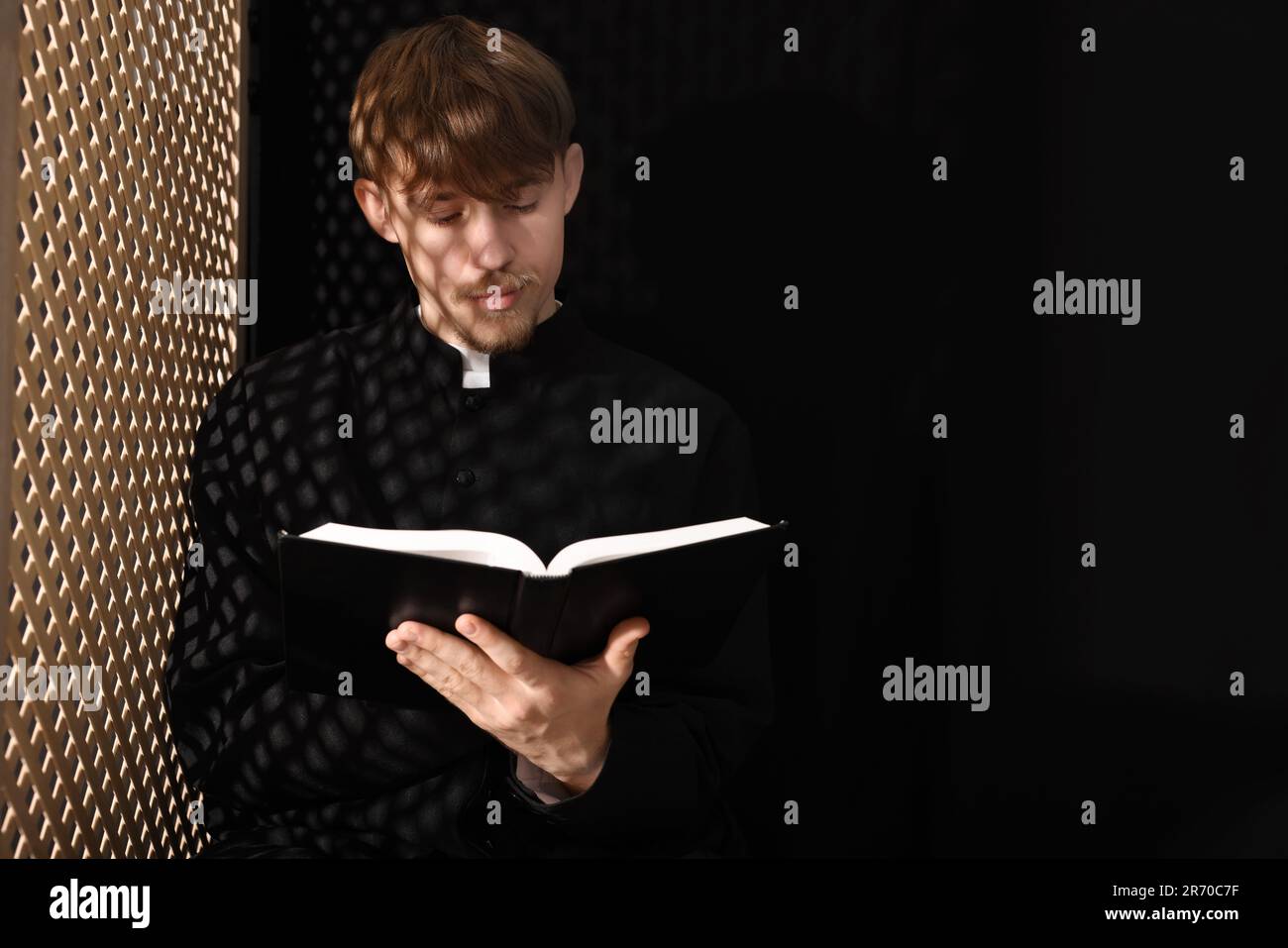 Catholic priest with Bible near wooden window in confessional. Space ...