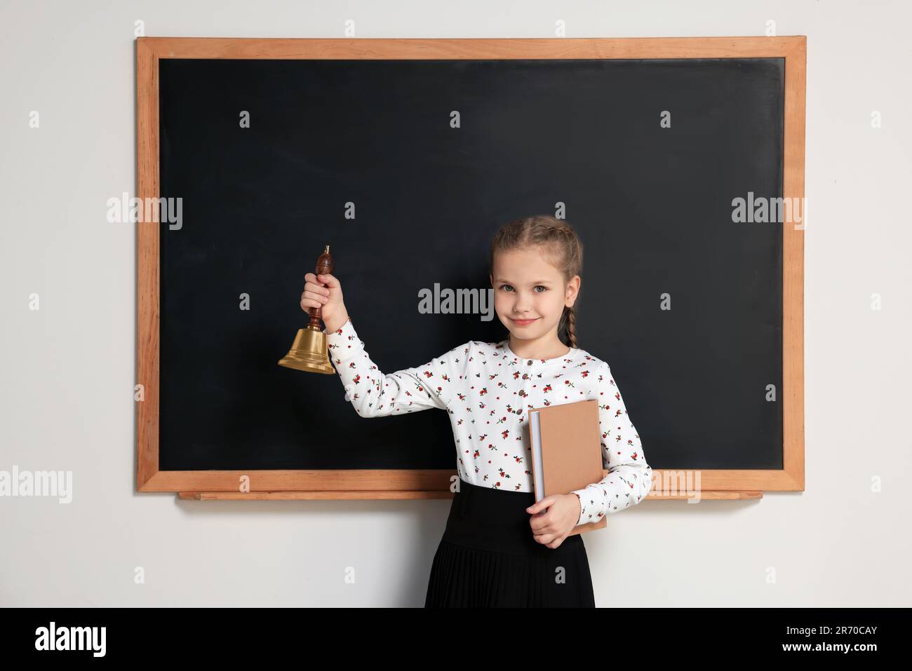Pupil with school bell near black chalkboard in classroom Stock Photo ...