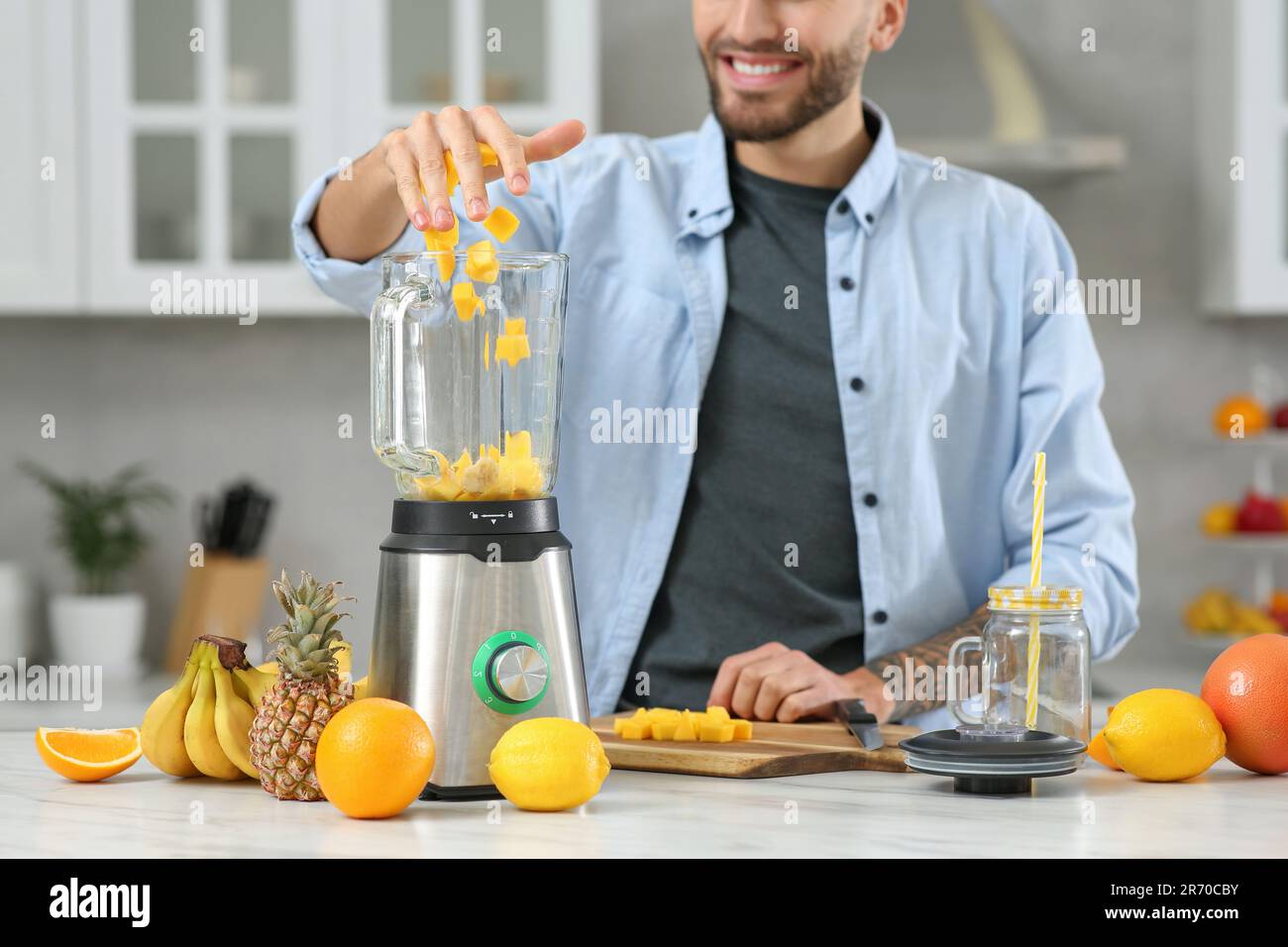 Man adding mango into blender with ingredients for smoothie in kitchen ...