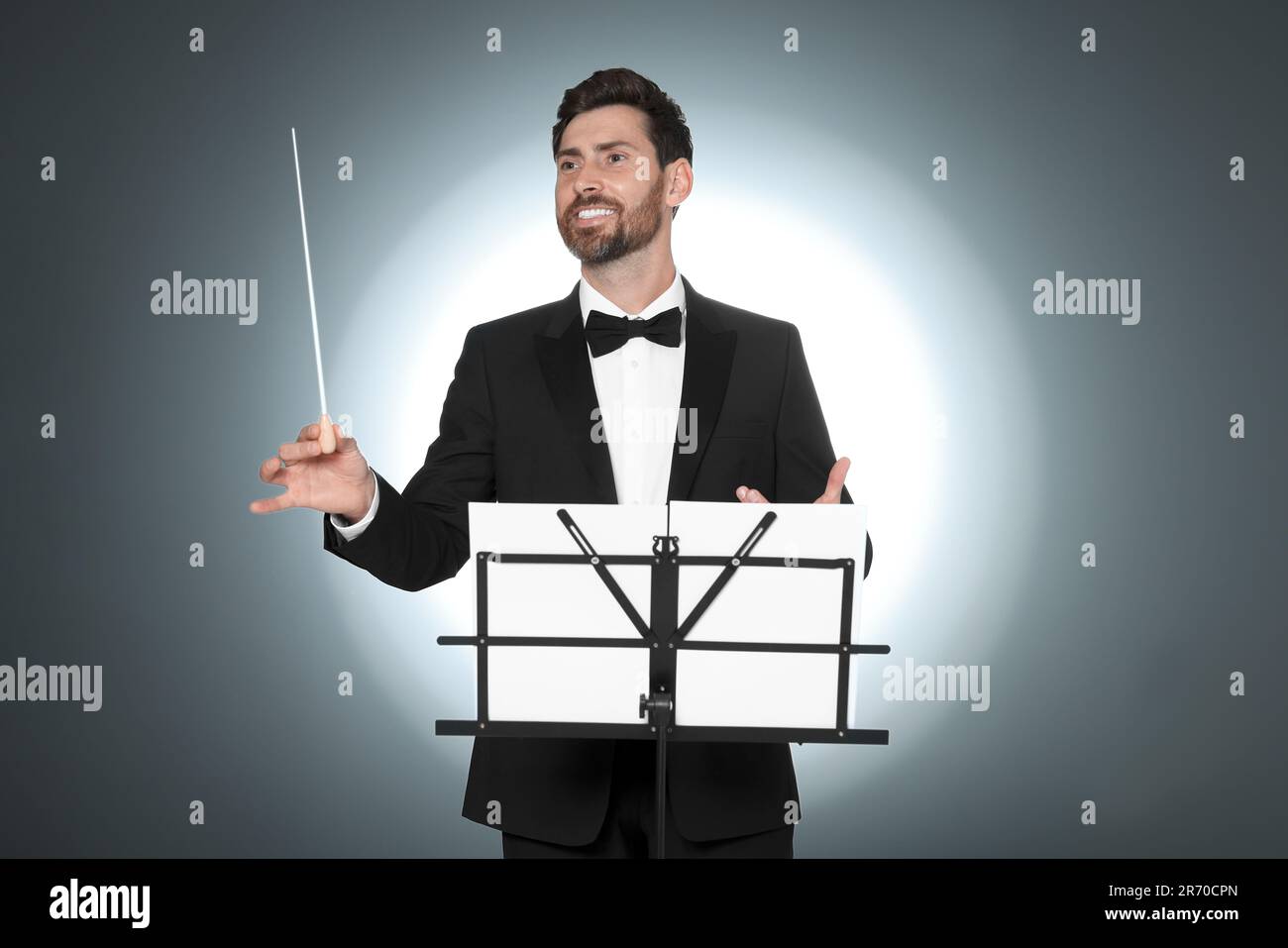 Happy professional conductor with baton and note stand on grey ...