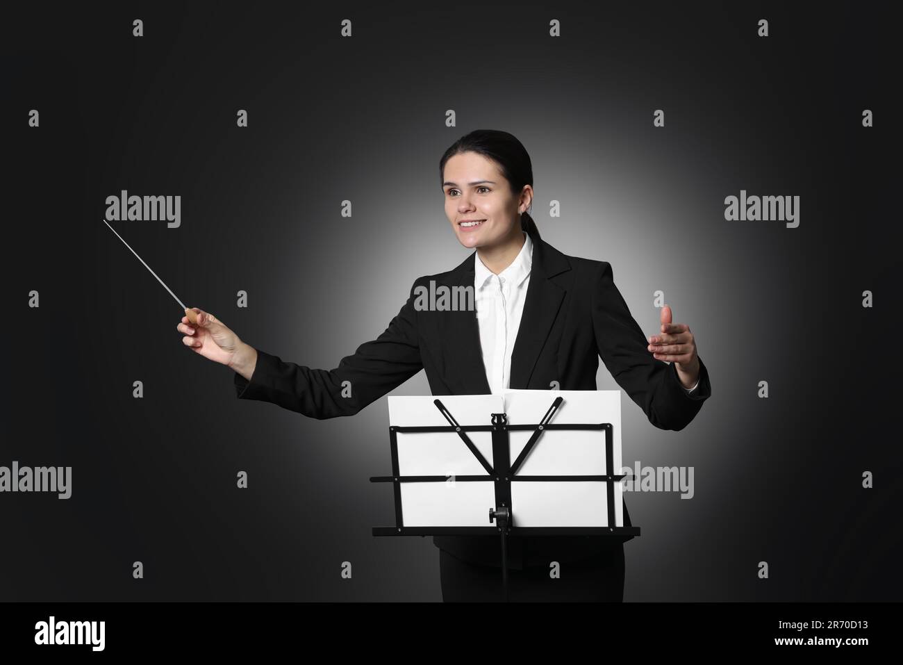 Happy professional conductor with baton and note stand on black ...