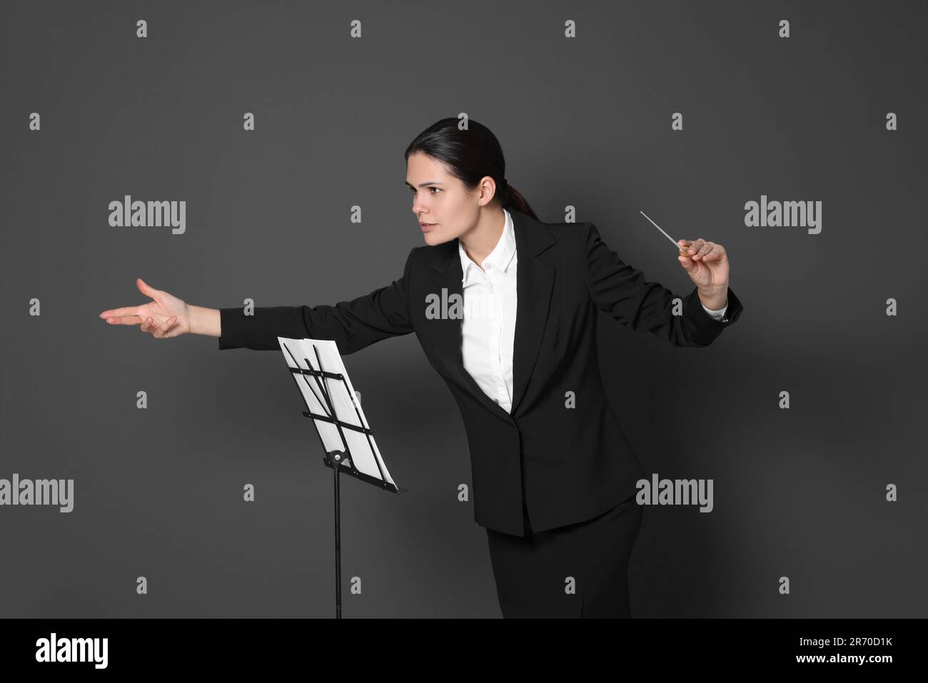 Happy professional conductor with baton and note stand on grey ...