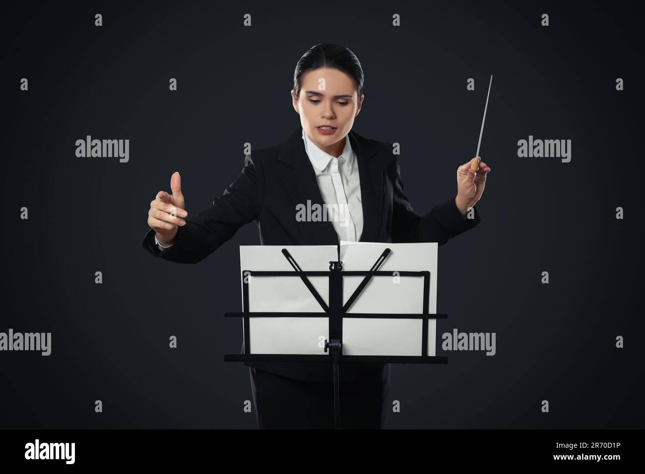 Professional conductor with baton and note stand on dark background ...