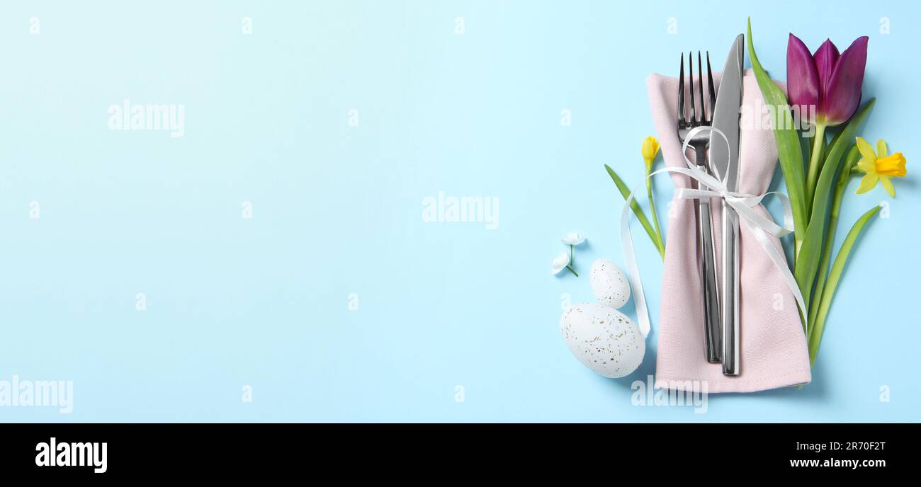 Set of cutlery, Easter eggs and flowers on light blue table, top view ...