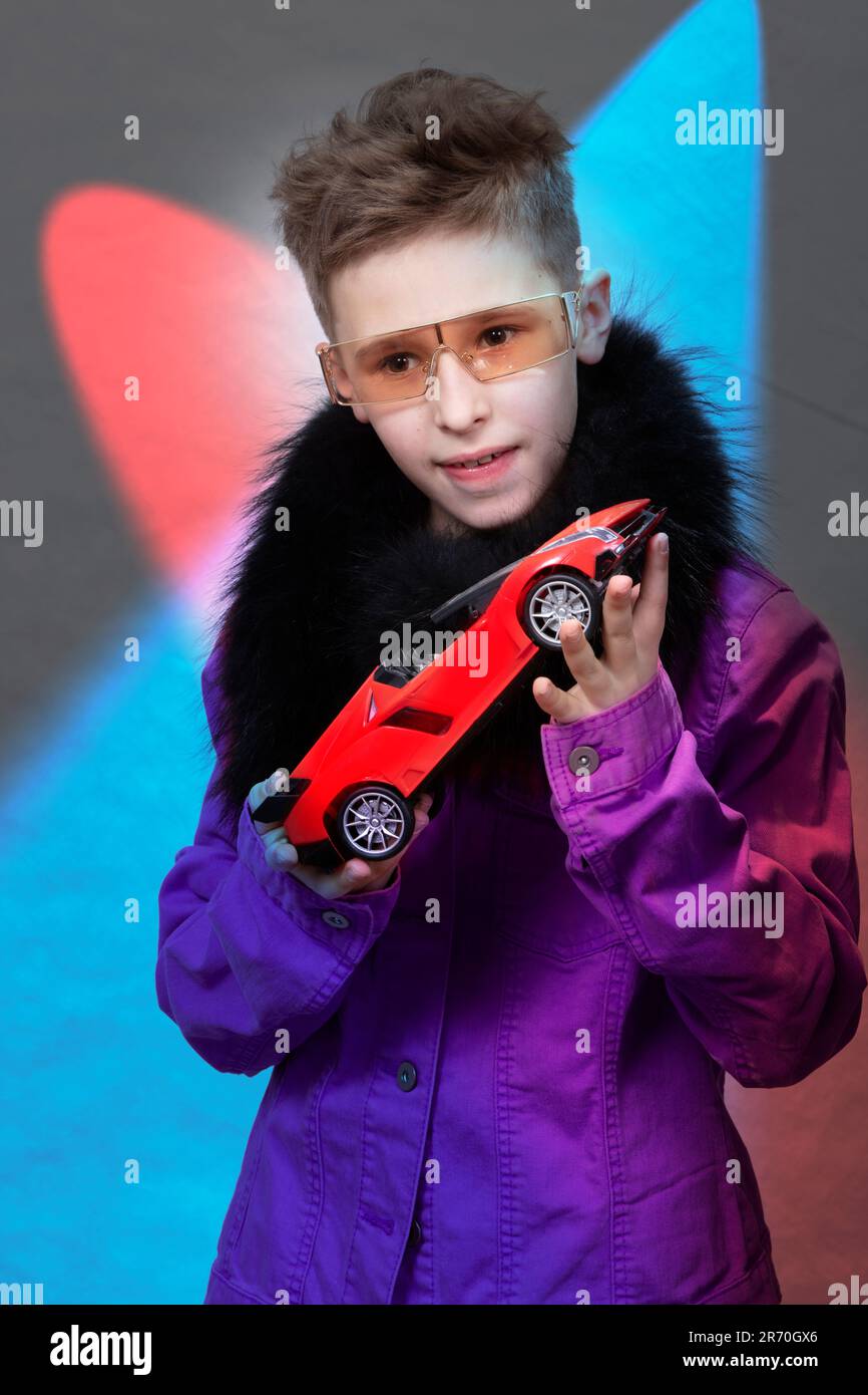 A fashionable boy is holding a toy car in his hands, on a multi-colored ...