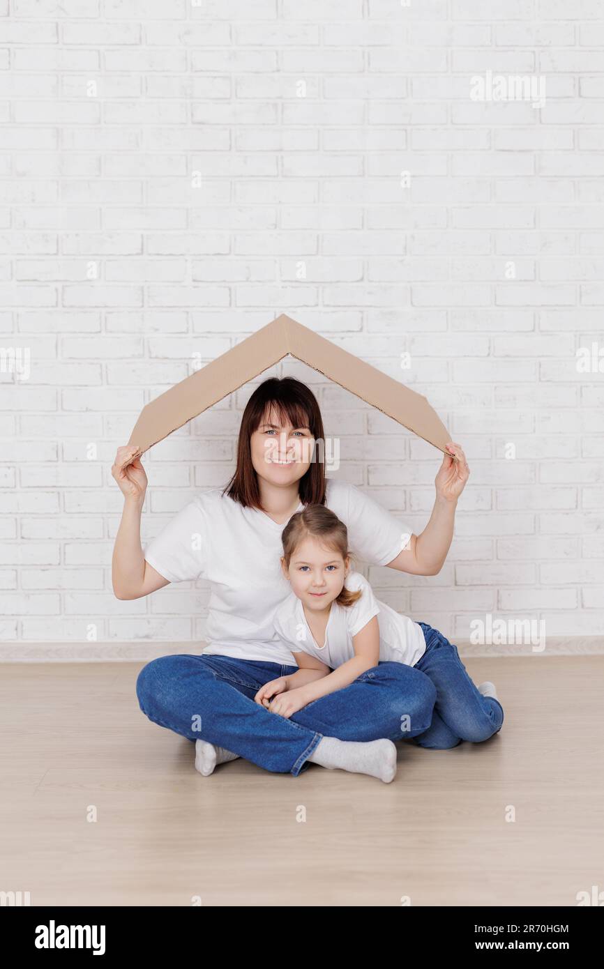 Happy woman and little girl sitting under cardboard roof on the floor ...