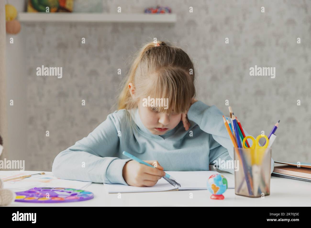 Exhausted schooler cute little girl sitting at desk, suffering from ...