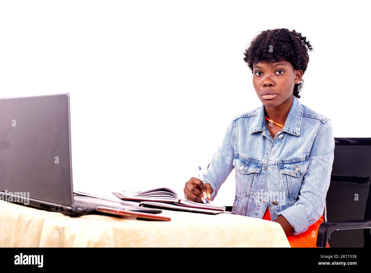 young student girl sitting on the table facing the laptop and writing ...