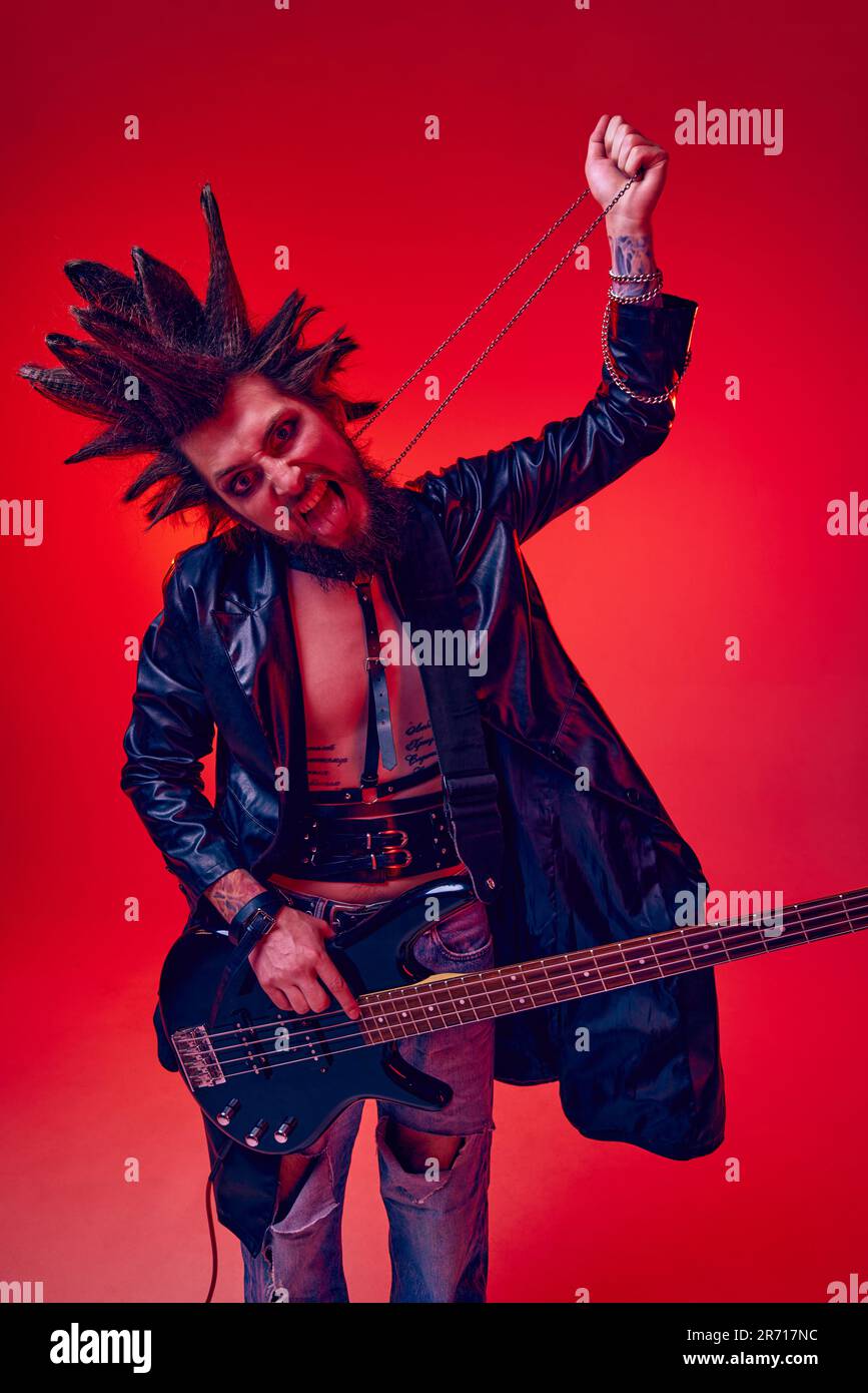 Young man, punk in extraordinary clothes and hairdo playing electric ...