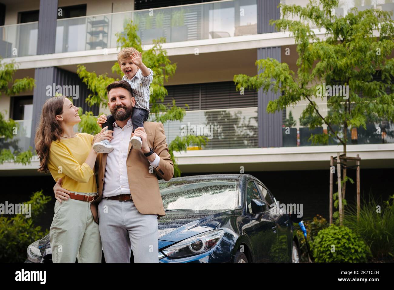 Happy family standing in front their electric car and charging it on ...