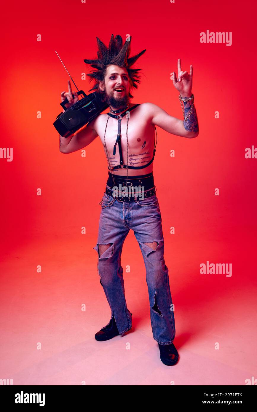 Young man, punk in extraordinary clothes and hair listening to music ...