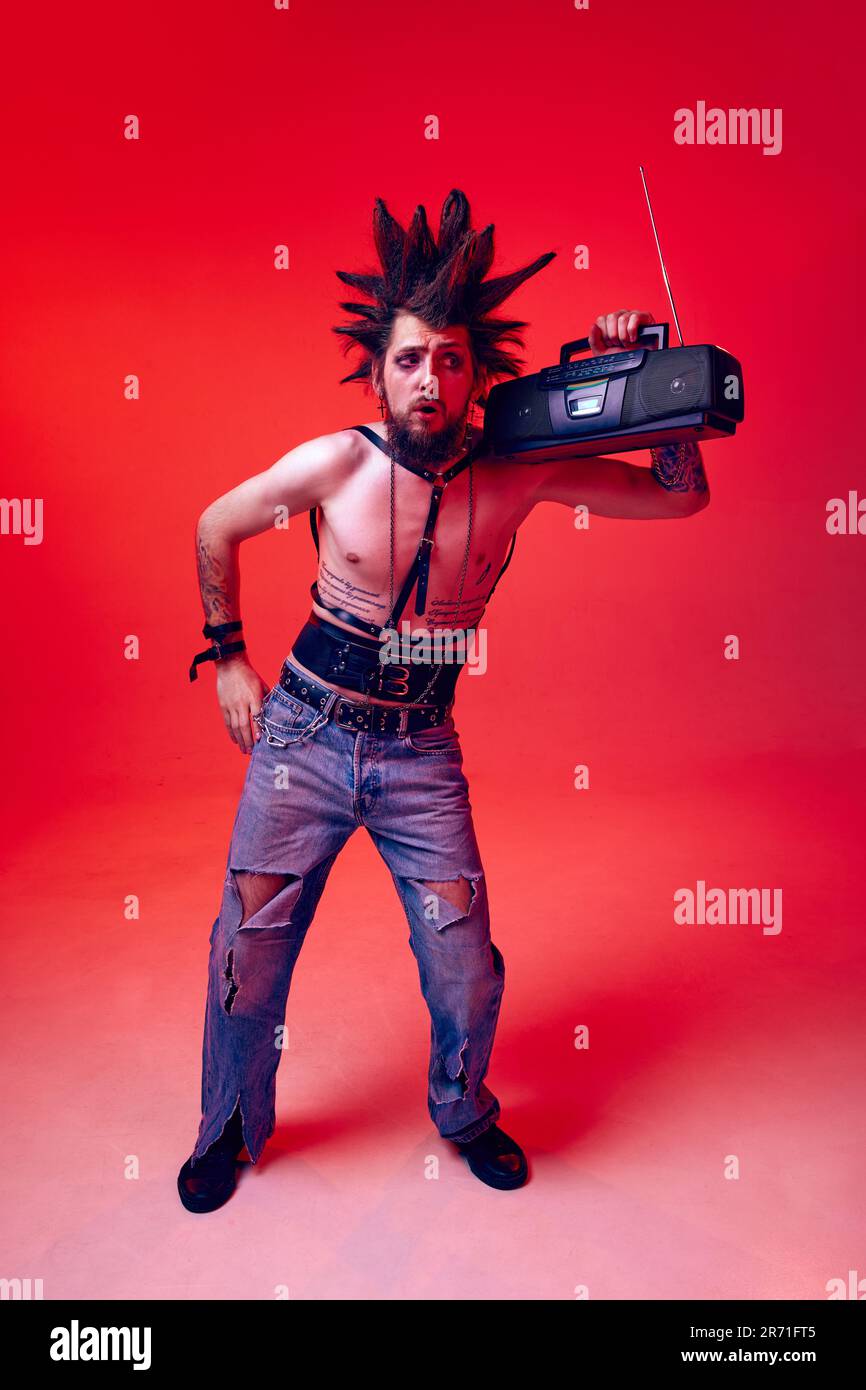 Young man, punk in extraordinary clothes and hair listening to music ...