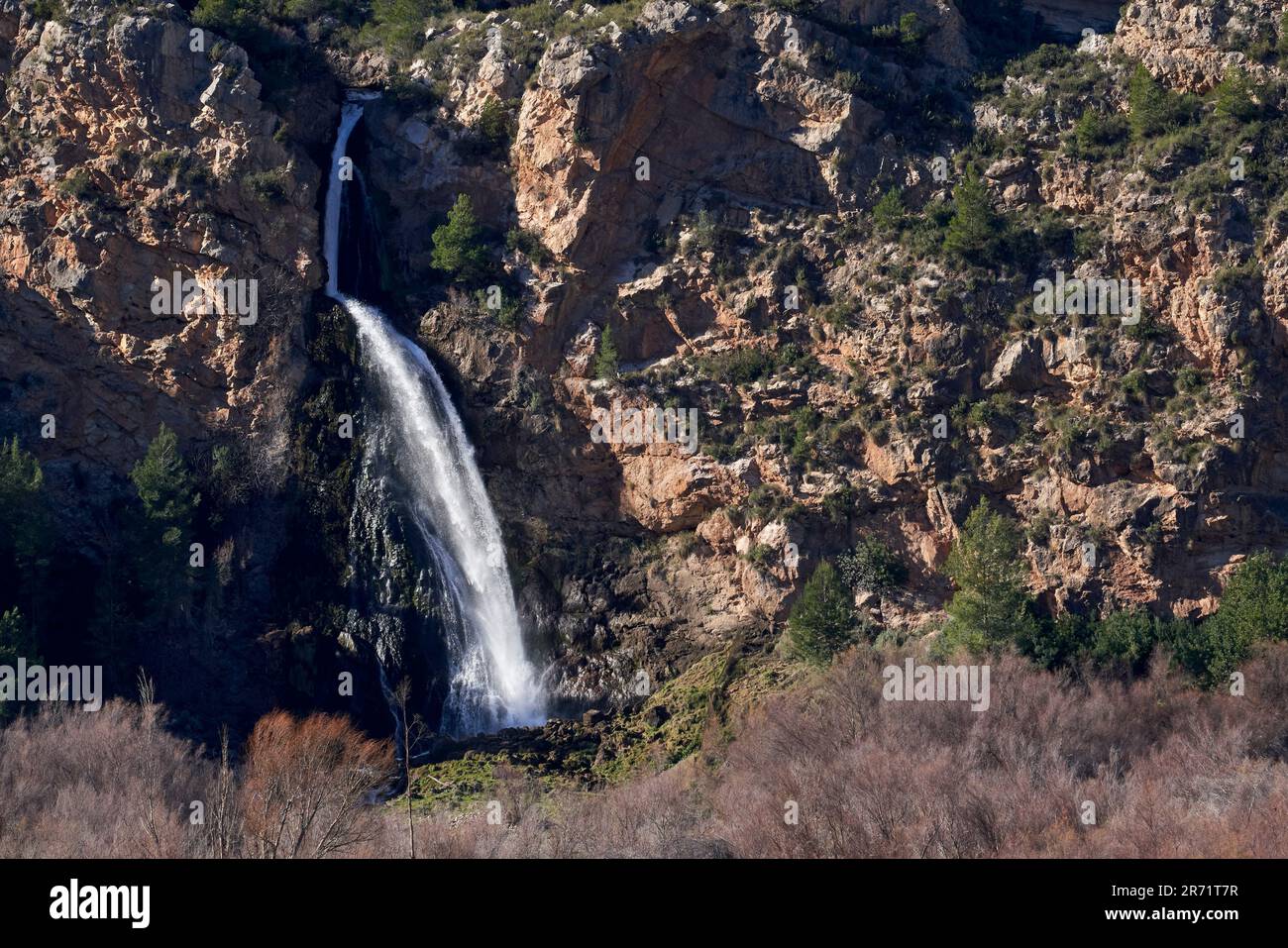 A majestic waterfall cascades down a rocky cliff face, creating a ...