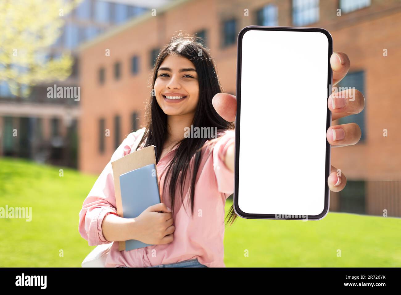 Happy hispanic student lady showing smartphone with empty screen and ...