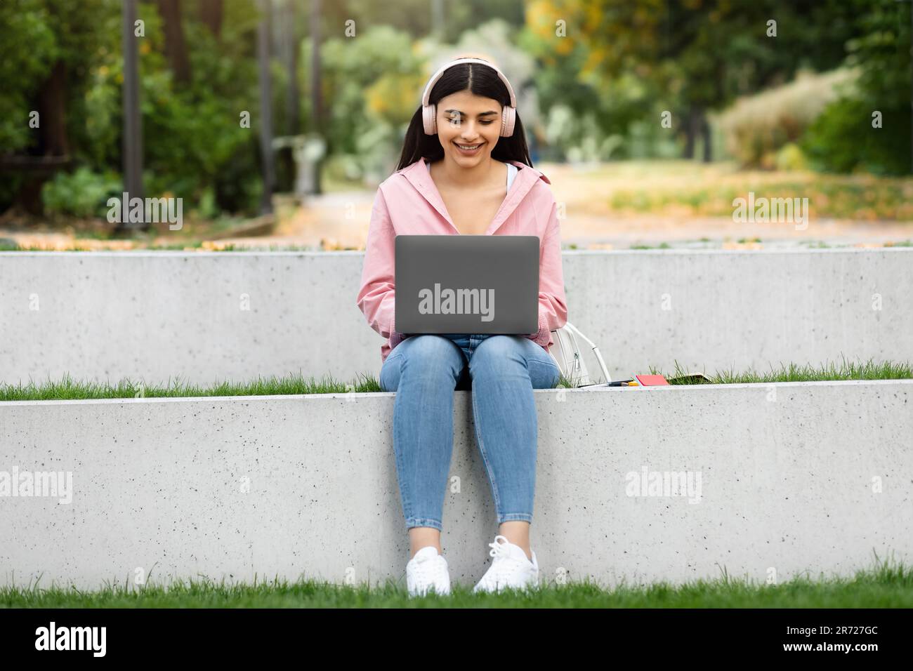 Happy teen student lady in wireless headphones using laptop, studying ...