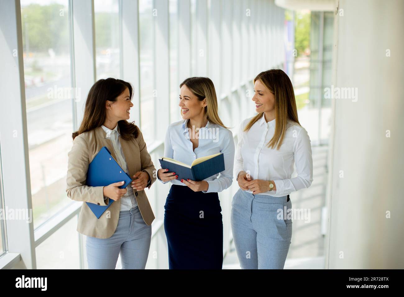 Three cute young business women having a discussion while walking in the office hallway Stock ...